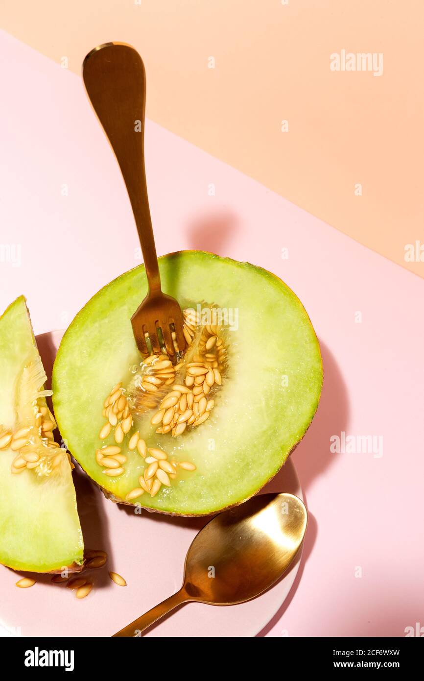 From above cut ripe appetizing sweet pitted melon on plate with spoon ...
