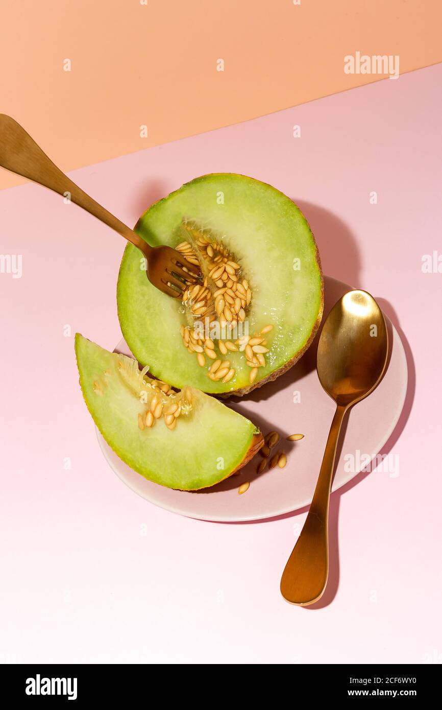 From above cut ripe appetizing sweet pitted melon on plate with spoon ...
