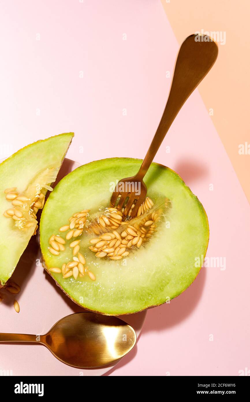 From above cut ripe appetizing sweet pitted melon on plate with spoon ...