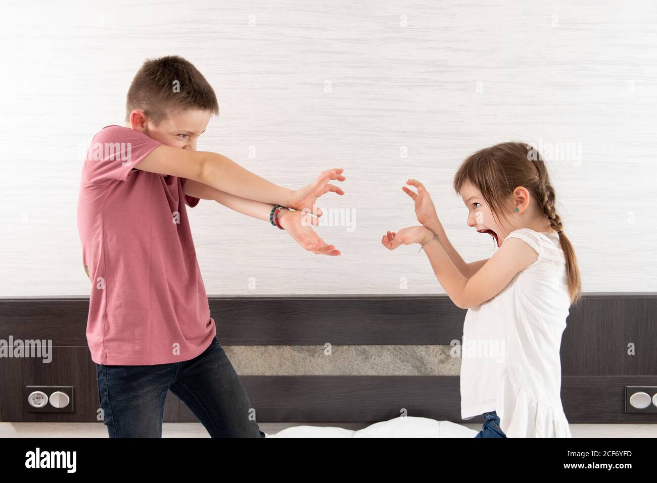 Side View Of Playful Brother And Sister Having Fun On Bedroom While