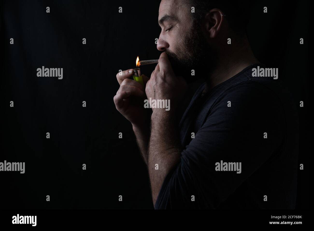 Side view of crop concentrated male smoker lighting up marijuana blunt ...
