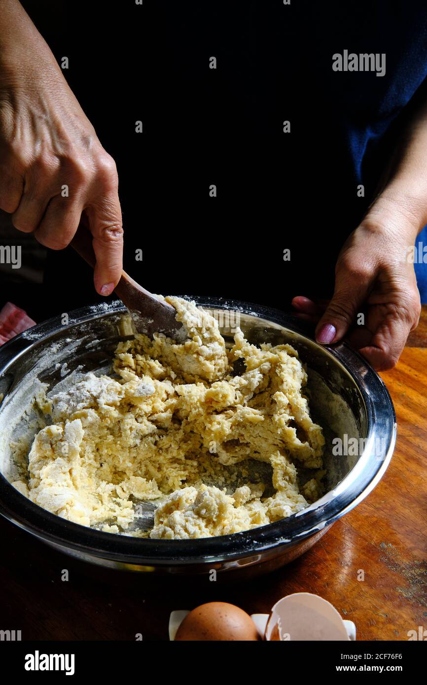 From above anonymous person using wooden spoon to mix soft pastry dough ...