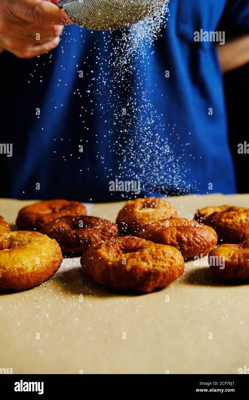 unrecognizable person using sieve to spill powdered sugar on stack of ...