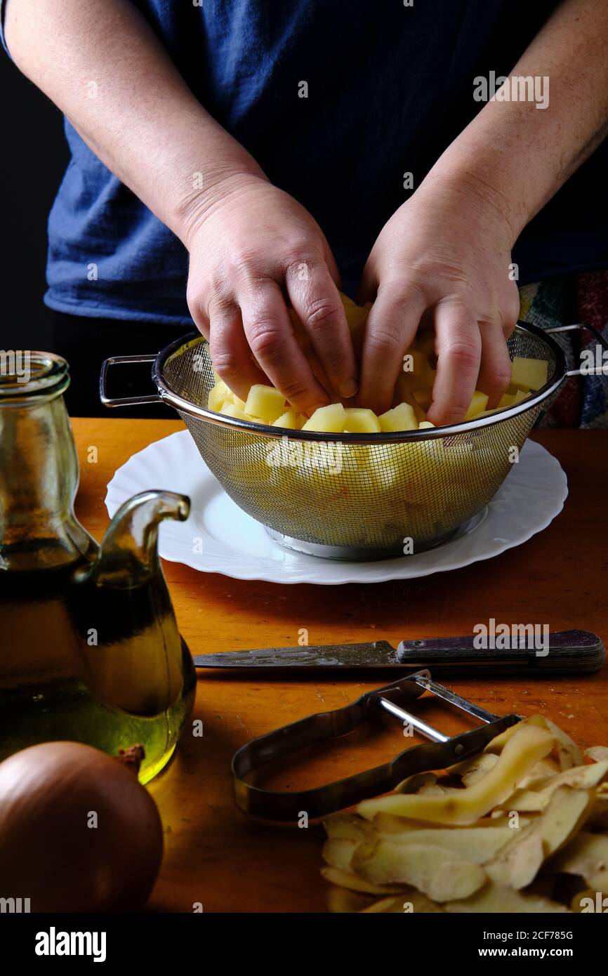 Crop female chef filtering fresh raw pieces of potatoes with sieve ...