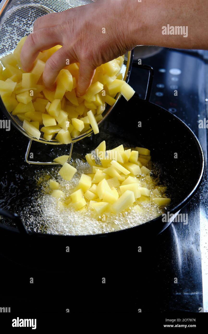 From above of crop chef pouring slices of potatoes from sieve to pan ...