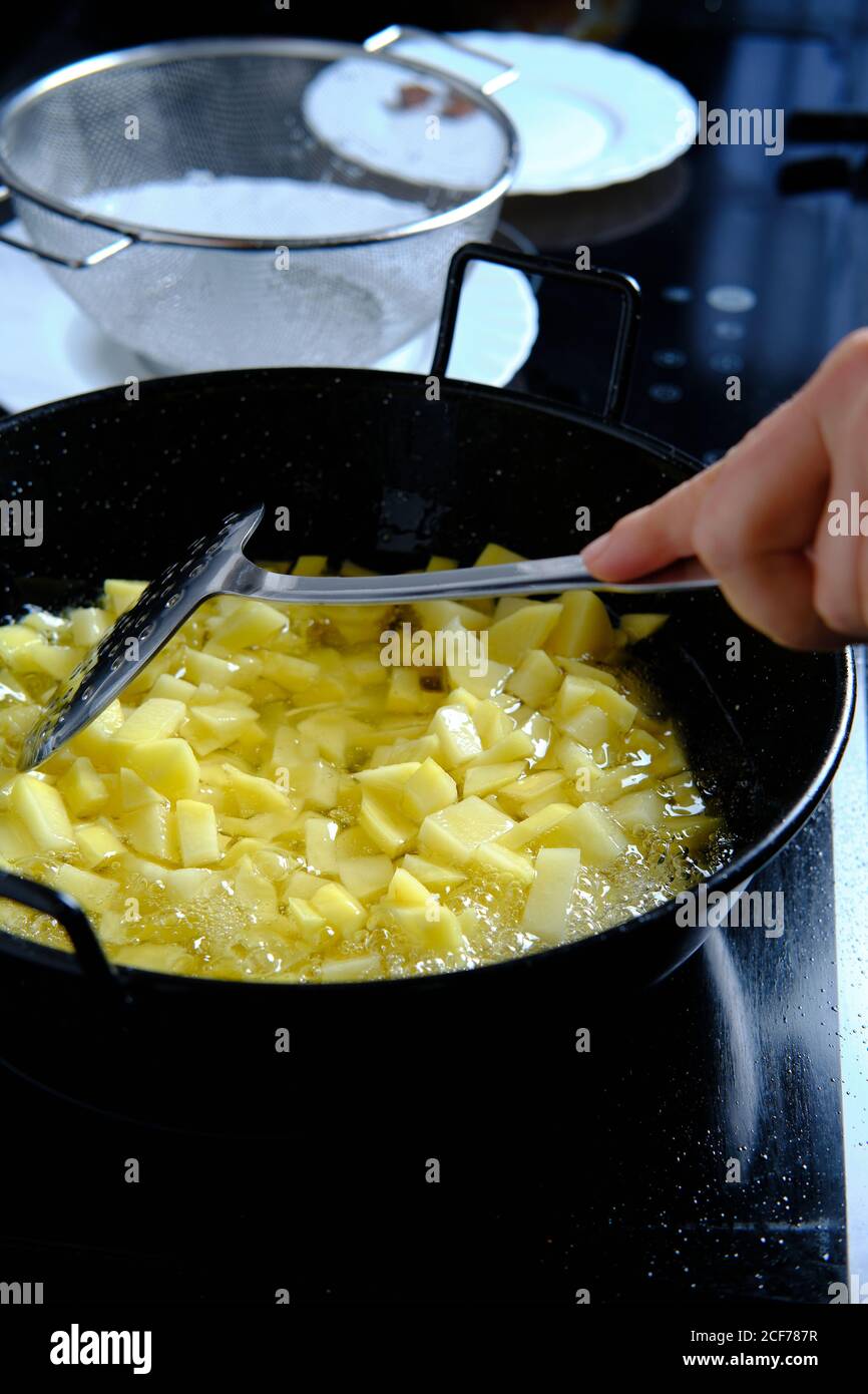 From above of crop chef pouring slices of potatoes from sieve to pan ...