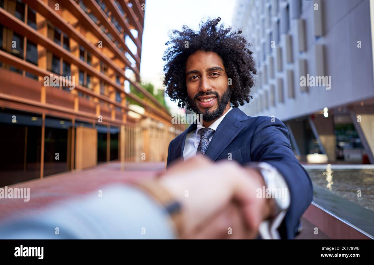 Ethnic happy businessman shaking hands with partner and looking at ...