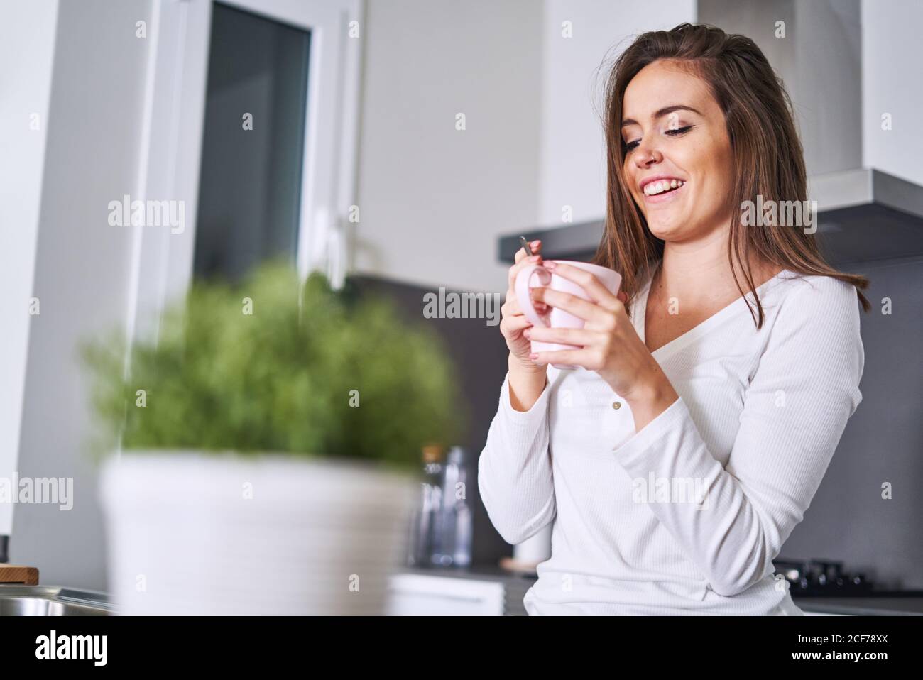 Side view of young attractive Woman drinking from mug in modern kitchen ...