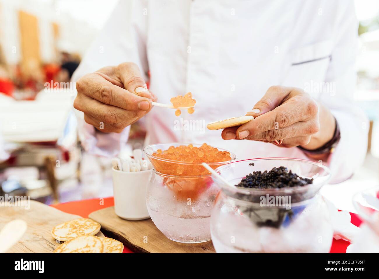 Crop unrecognizable person putting red caviar on small flatbread while ...