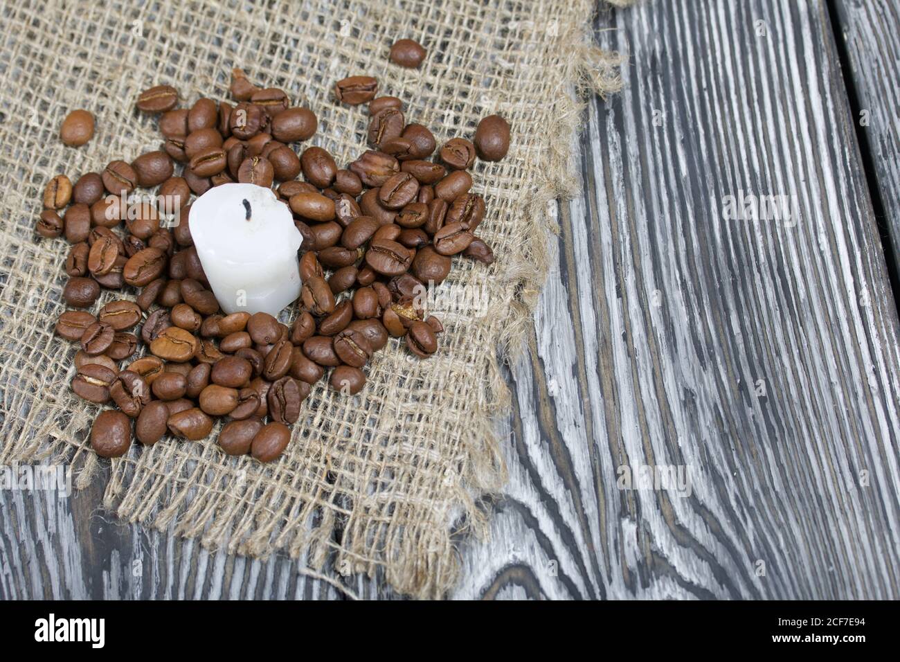 Coffee beans on rough linen and candle stub. On a surface of brushed ...