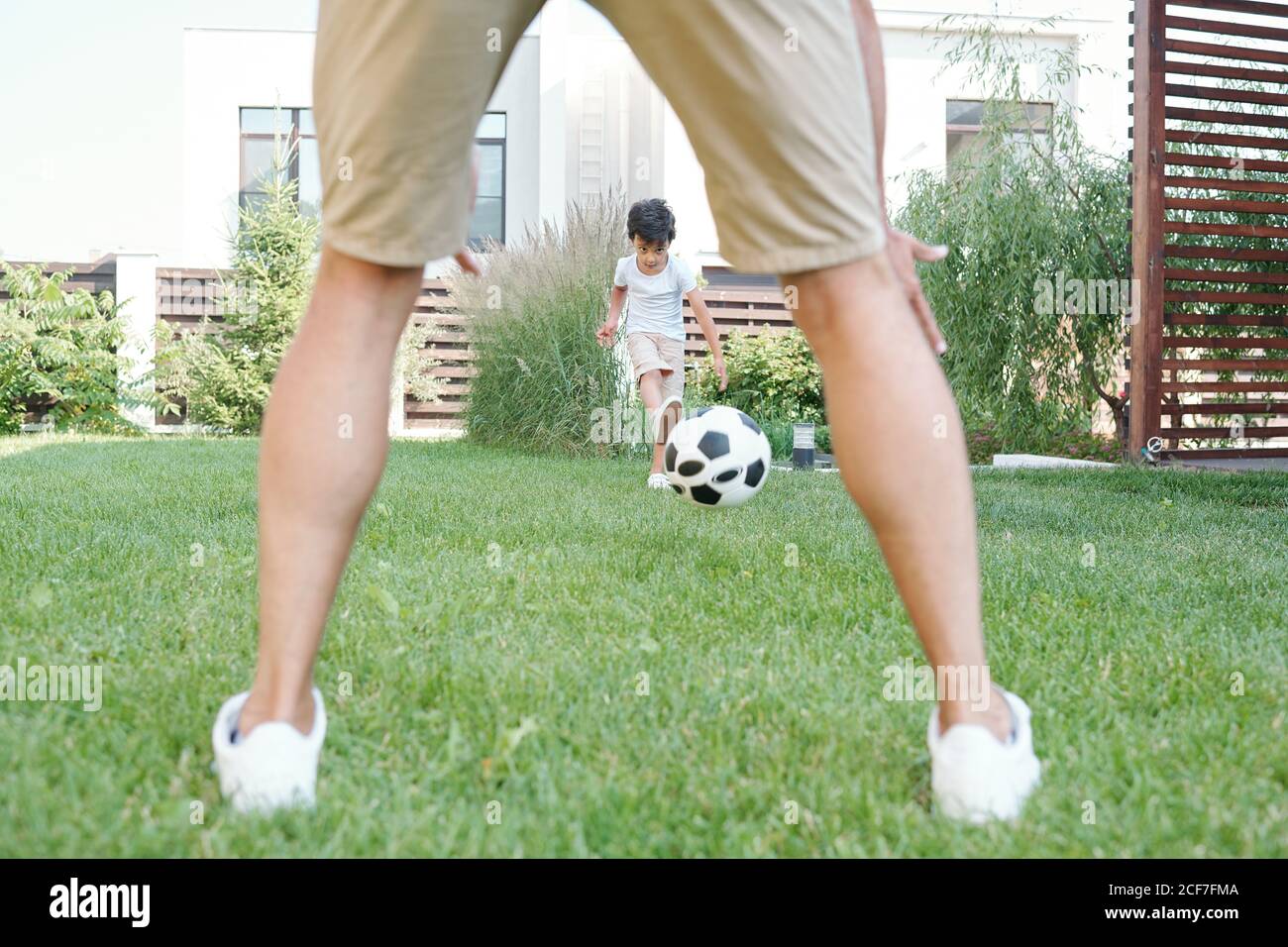 Unrecognizable man playing football with active boy on green grass in ...