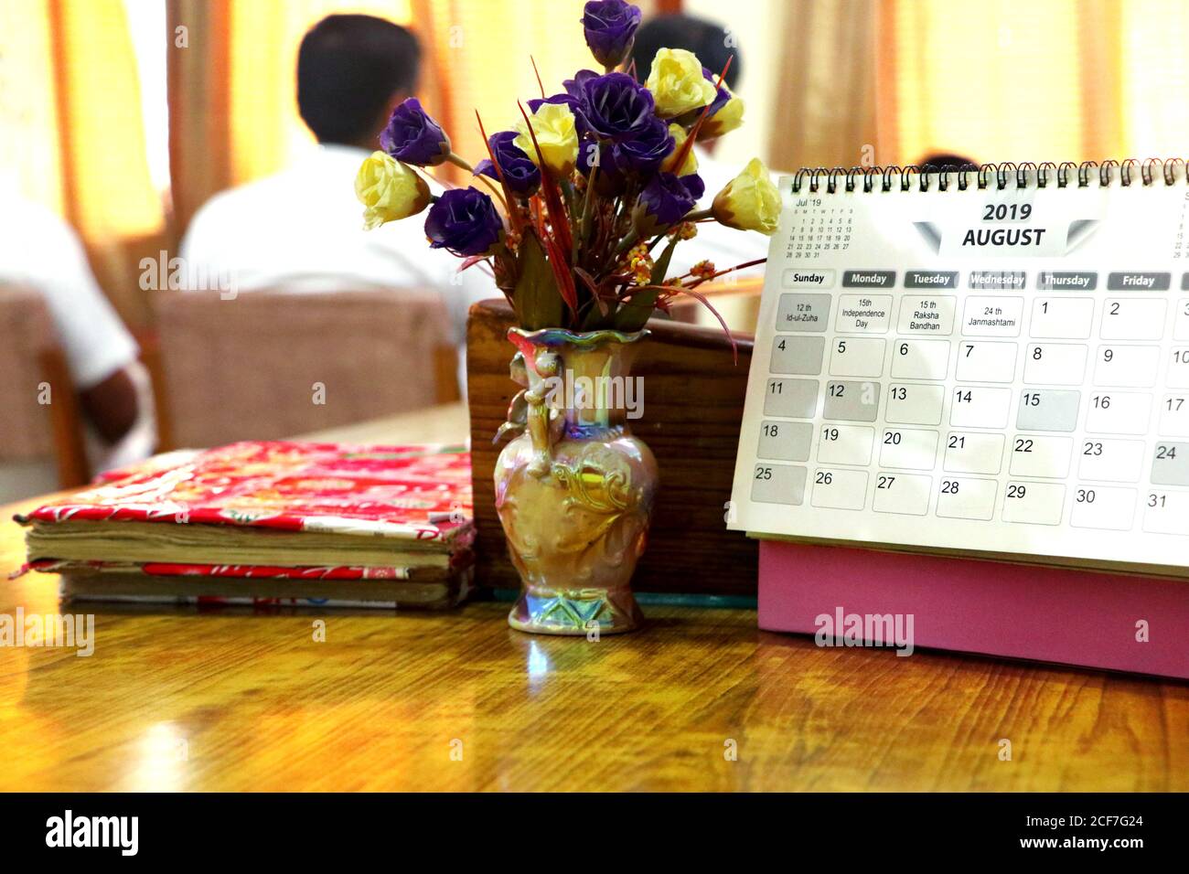 Closeup of a calendar, a small vase full of flowers, and notebooks on a ...