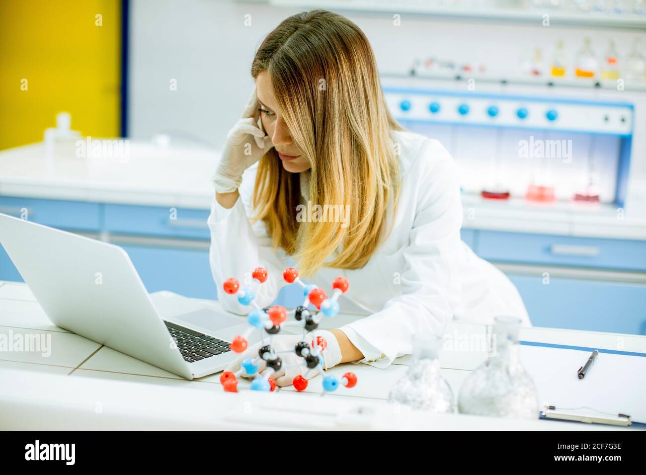Cute female researcher in white lab coat using laptop while working in ...