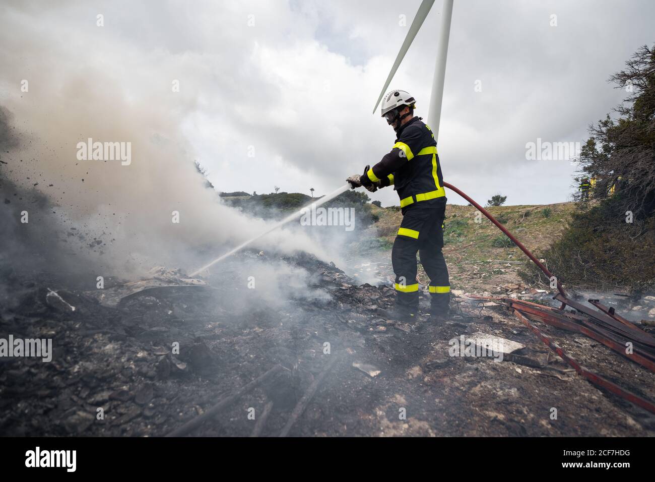 Side view of brave fireman in protective uniform standing with hose and ...
