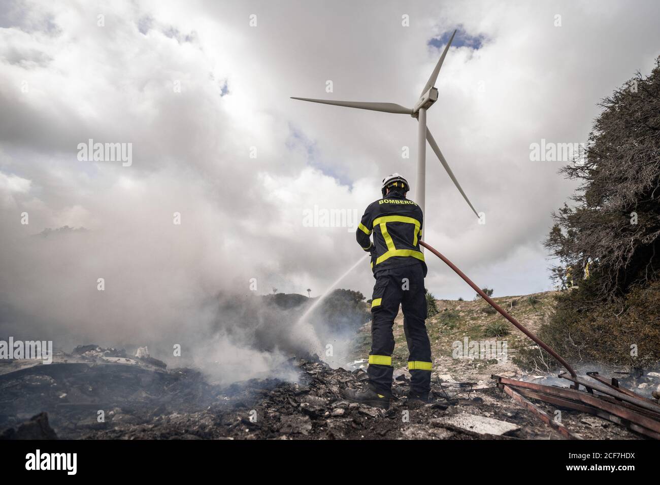 Back view of brave fireman in protective uniform standing with hose and ...