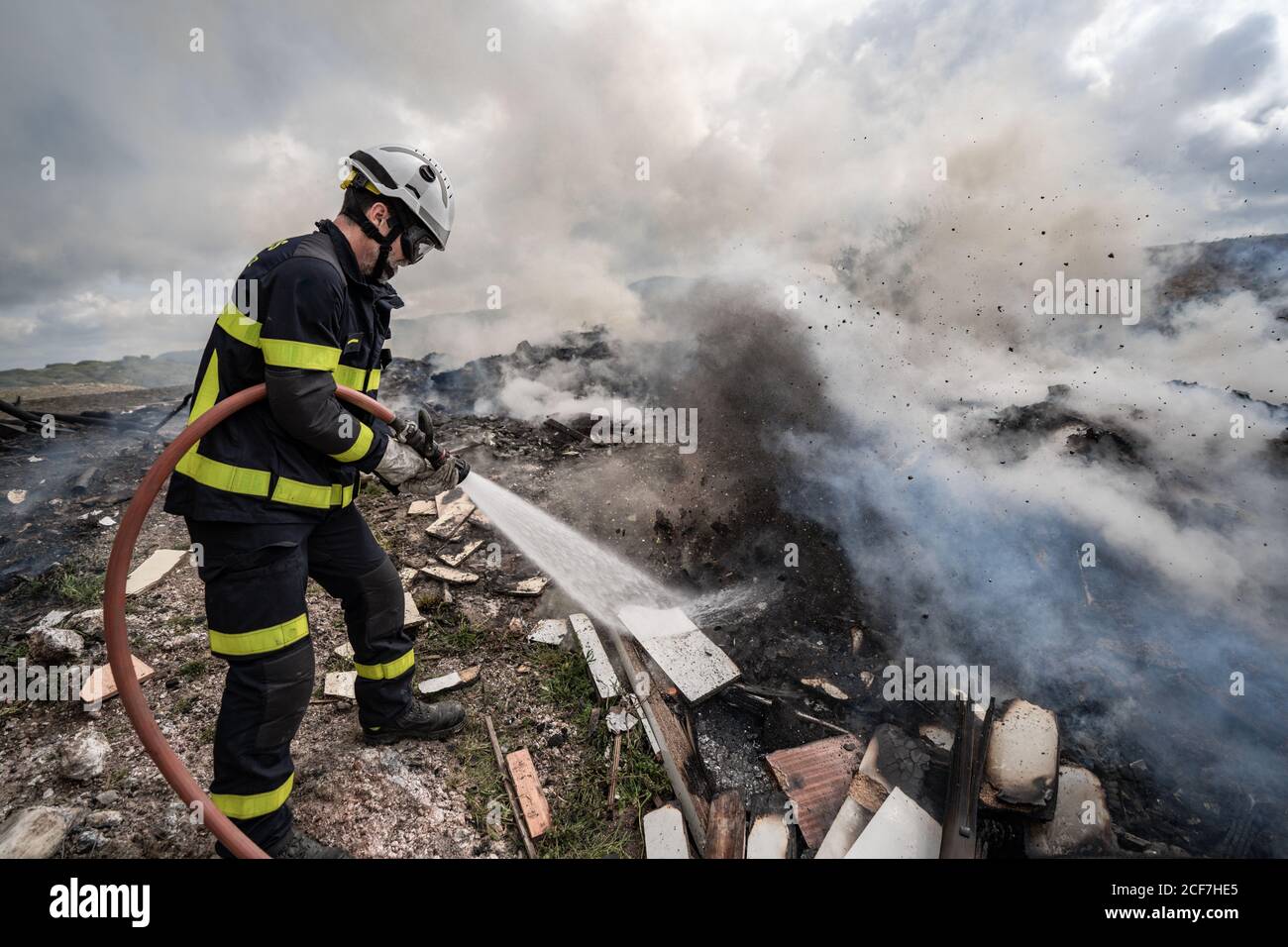 Side view of brave fireman in protective uniform standing with hose and ...