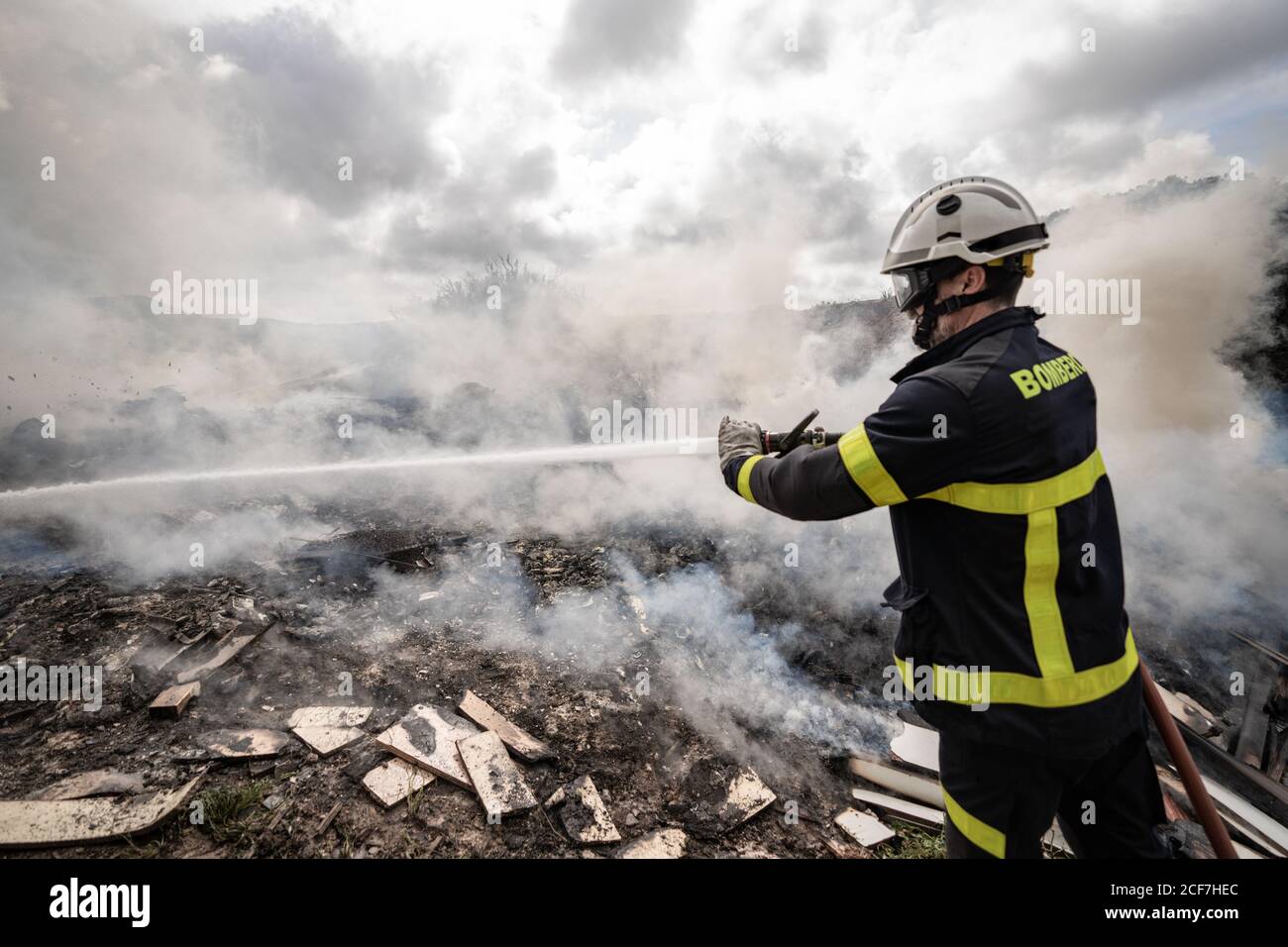 Side view of brave fireman in protective uniform standing with hose and ...