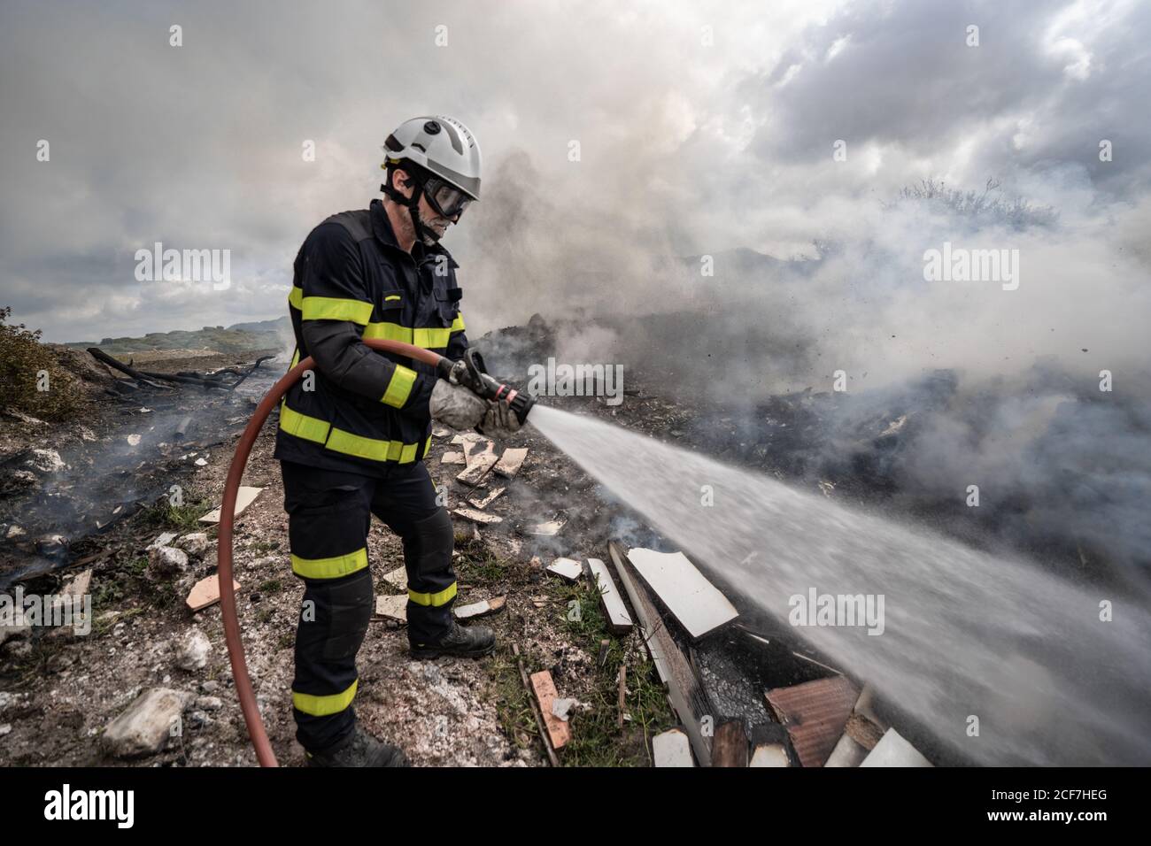 Side view of brave fireman in protective uniform standing with hose and ...