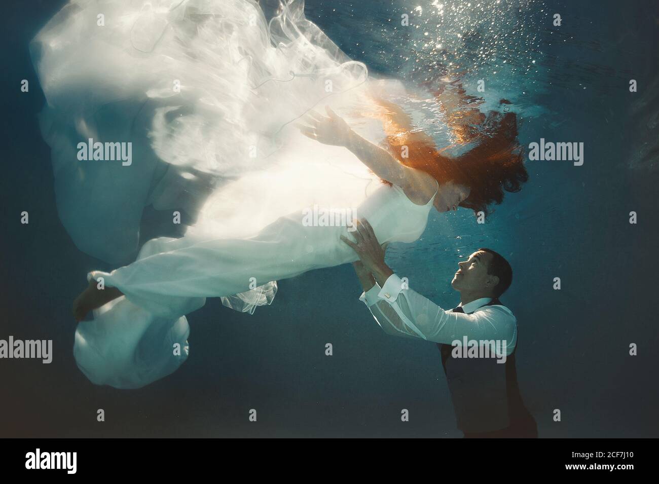 Side view of couple swimming together underwater in swimming pool after ...