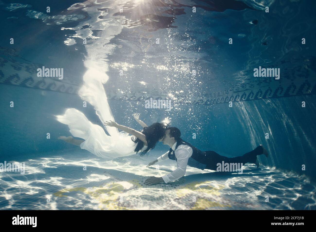 Side view of couple swimming together underwater in swimming pool after ...