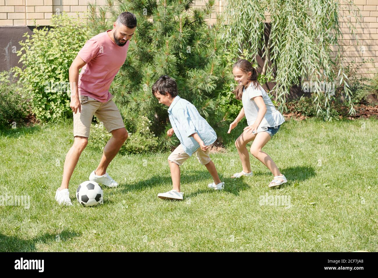 Modern father playing football with his son and daughter on lawn in ...