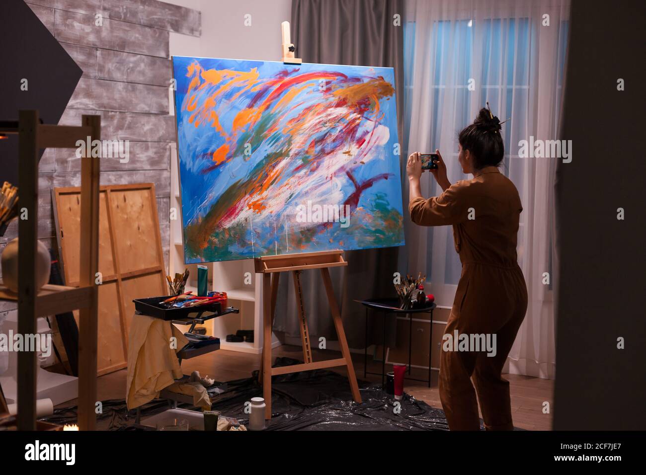 Artist using phone to take a photo of her masterpiece painting in art ...