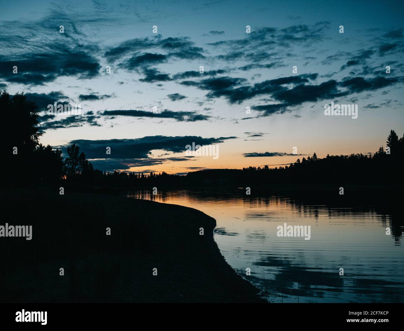 Beautiful evening sunset landscape with lake and dark forest and cloudy ...