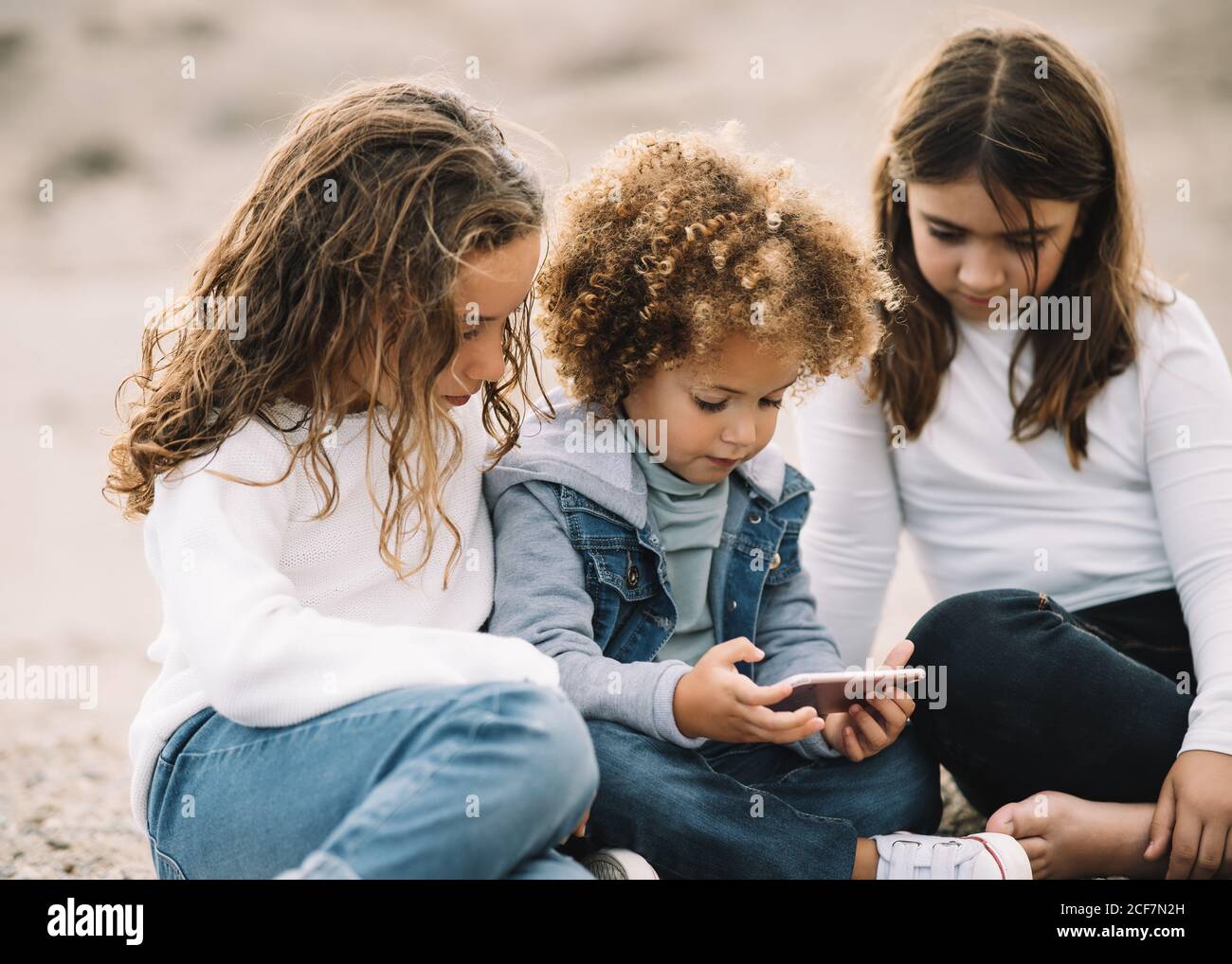 Concentrated kids dressed in casual clothes relaxing on sandy ground ...