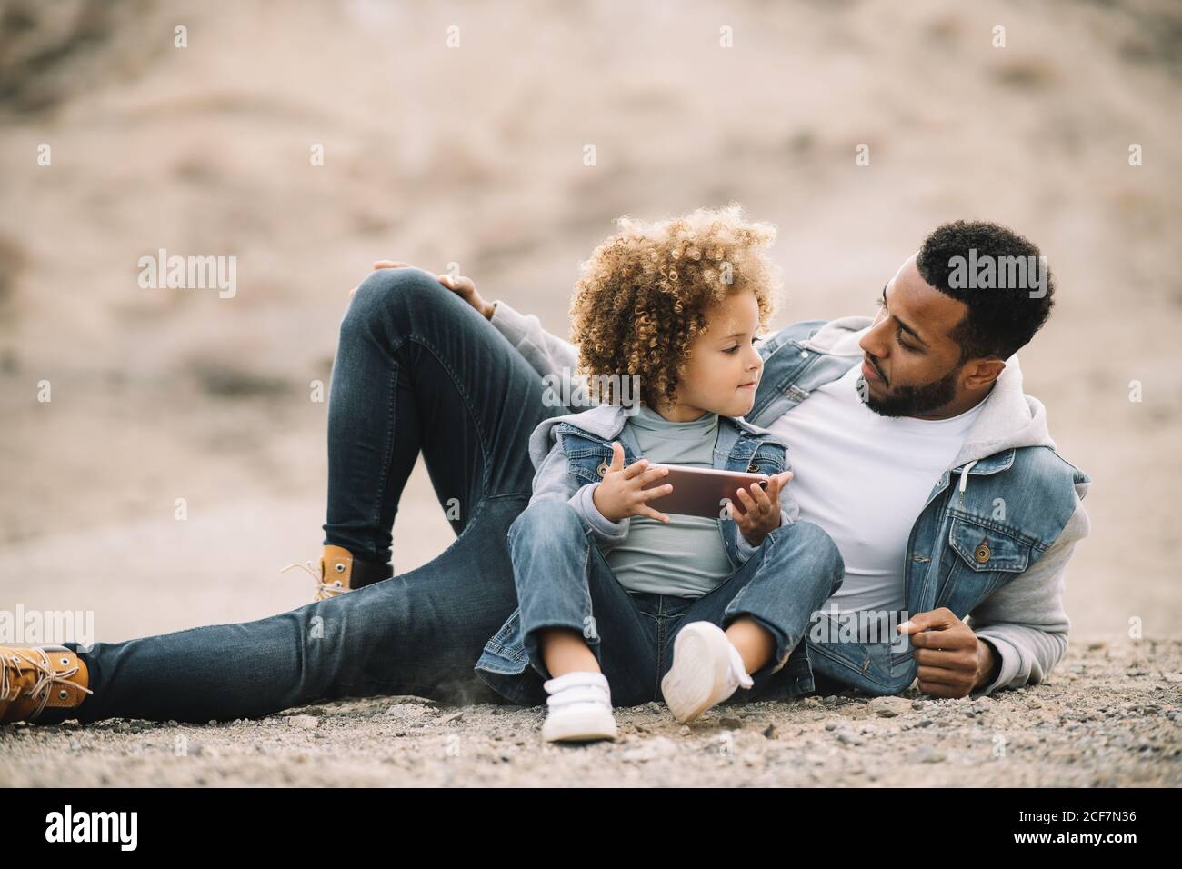 African American bearded casual man lying on sandy ground leaning on ...