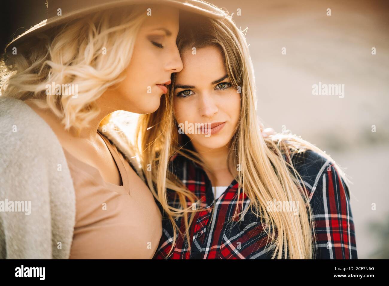 Woman in hat wearing casual clothes tenderly hugging female with long ...