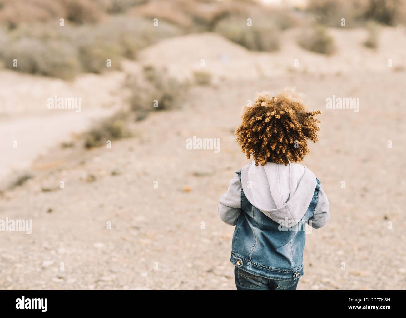 Back view of anonymous curly ethnic child dressed in casual clothes on ...