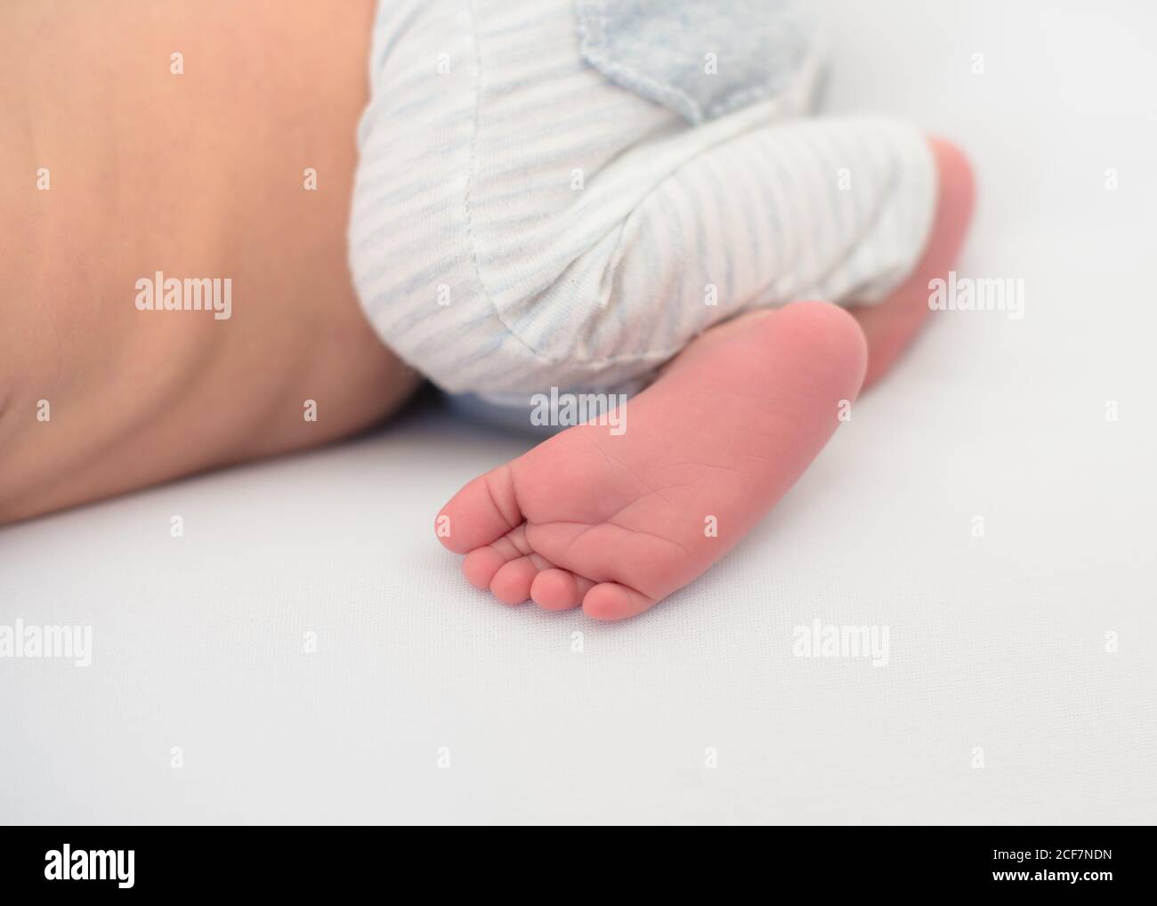 unrecognizable barefoot baby lying crossed legged on white sheet and ...