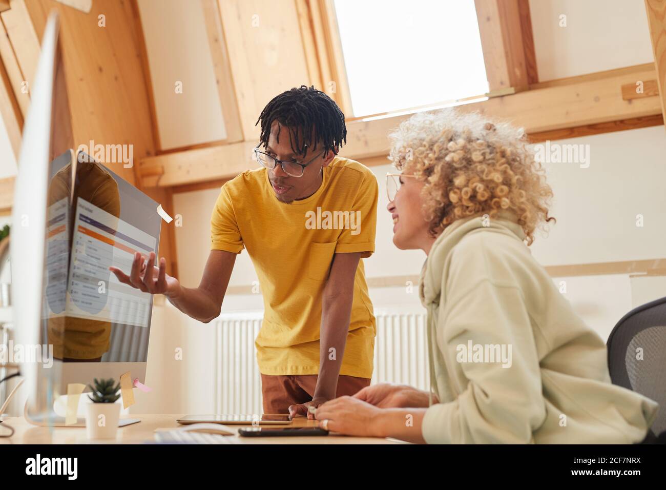 African man pointing at monitor of computer and talking to woman they ...