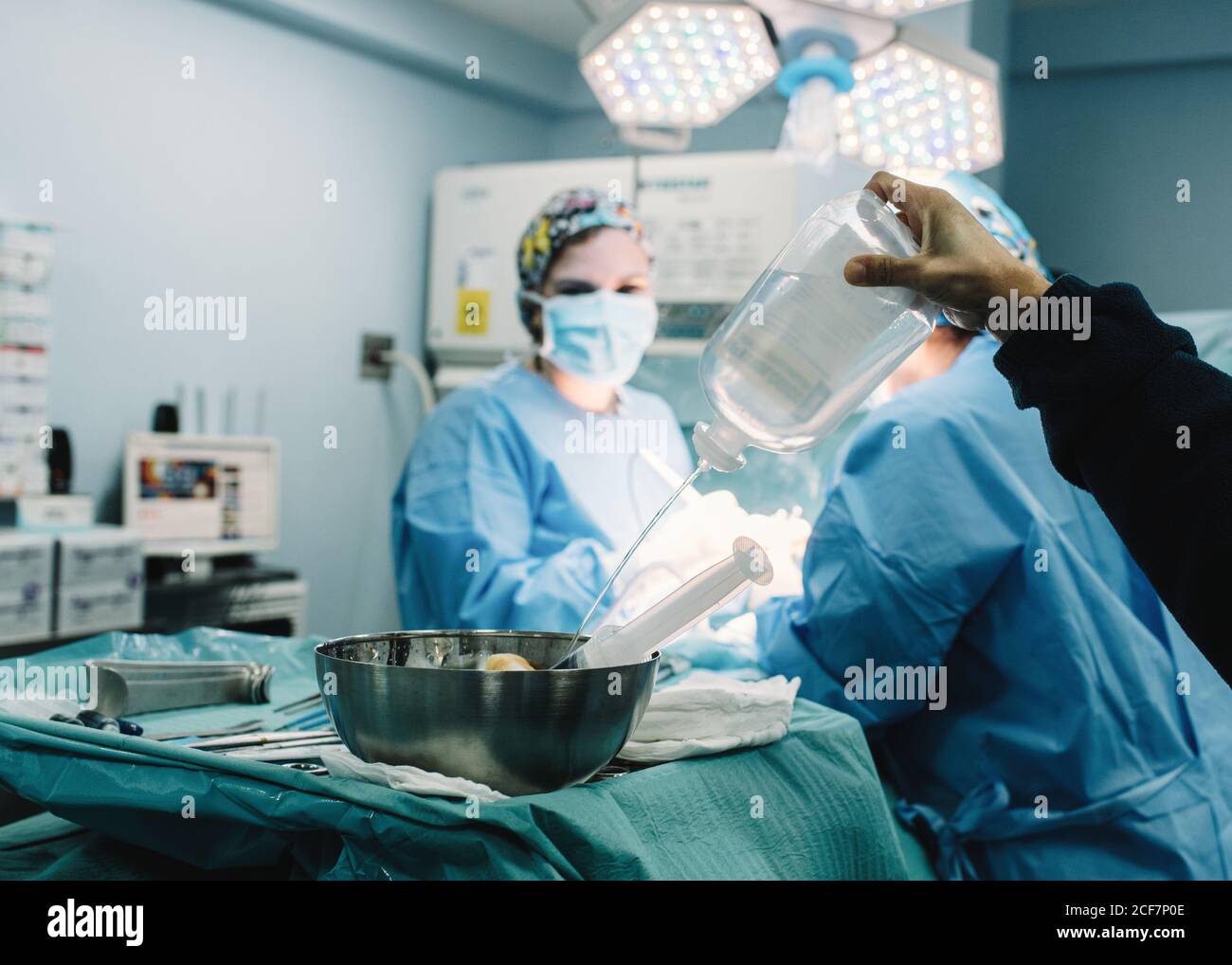 Crop hand pouring saline solution into bowl with syringe while doctors ...