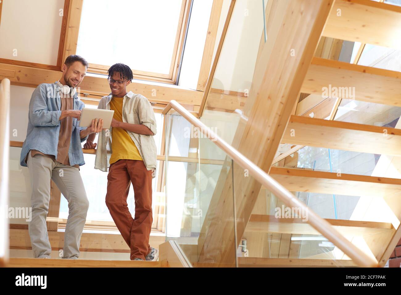 Two men standing on stairs watching something on digital tablet and ...