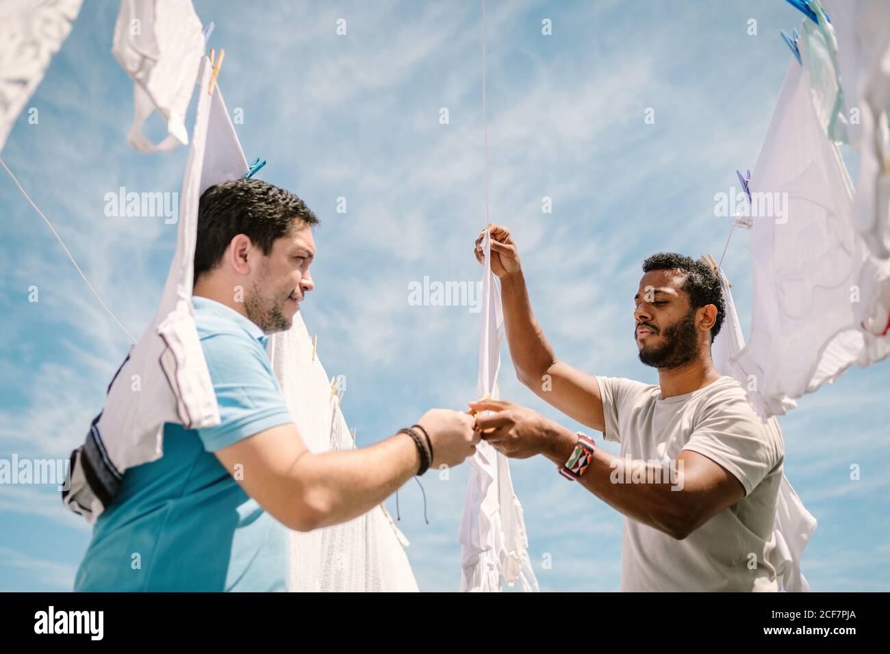 Multiracial men hanging clothes in bright day Stock Photo - Alamy