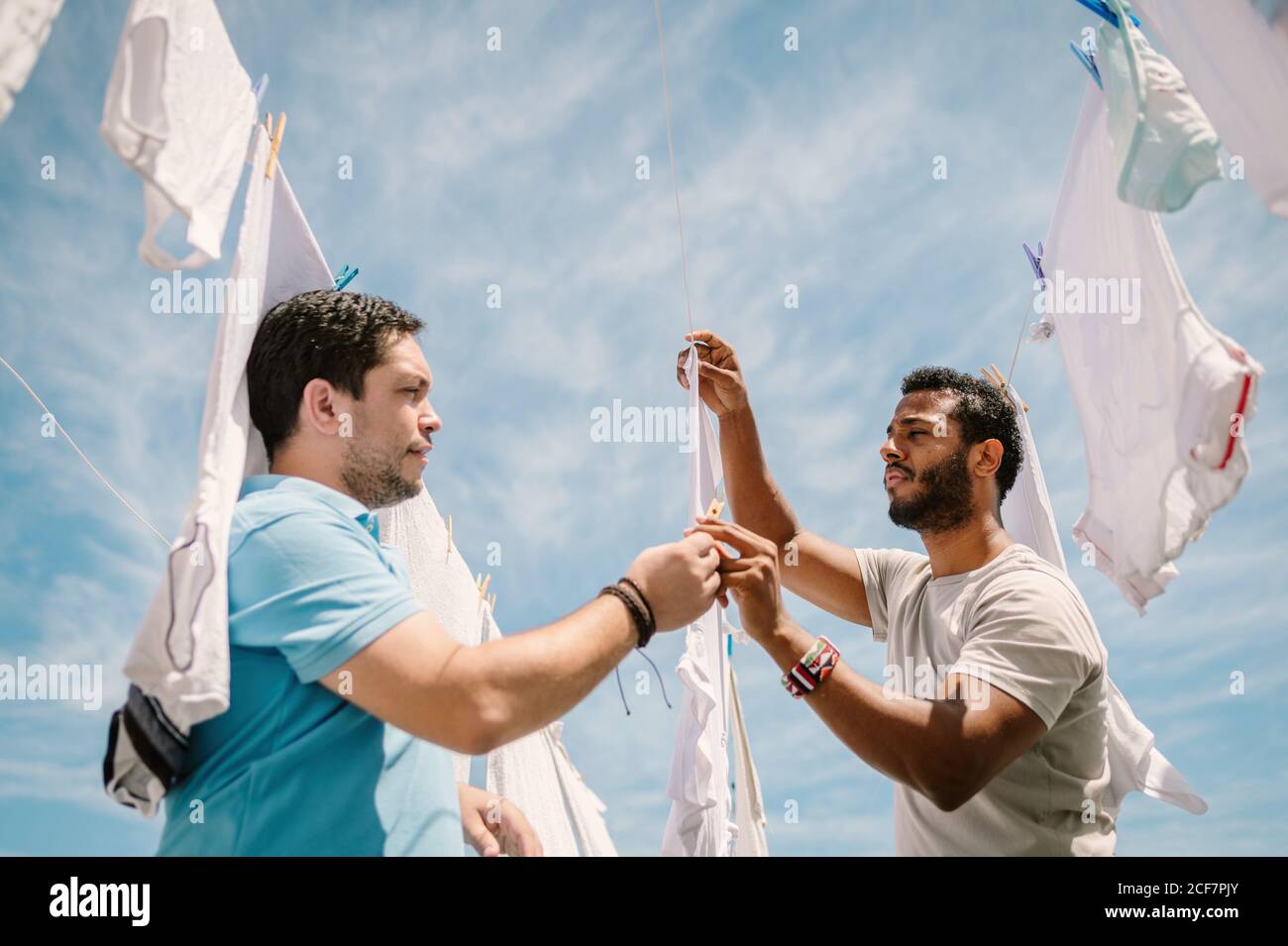 Side view of handsome bearded multi ethnic men hanging white clothes ...