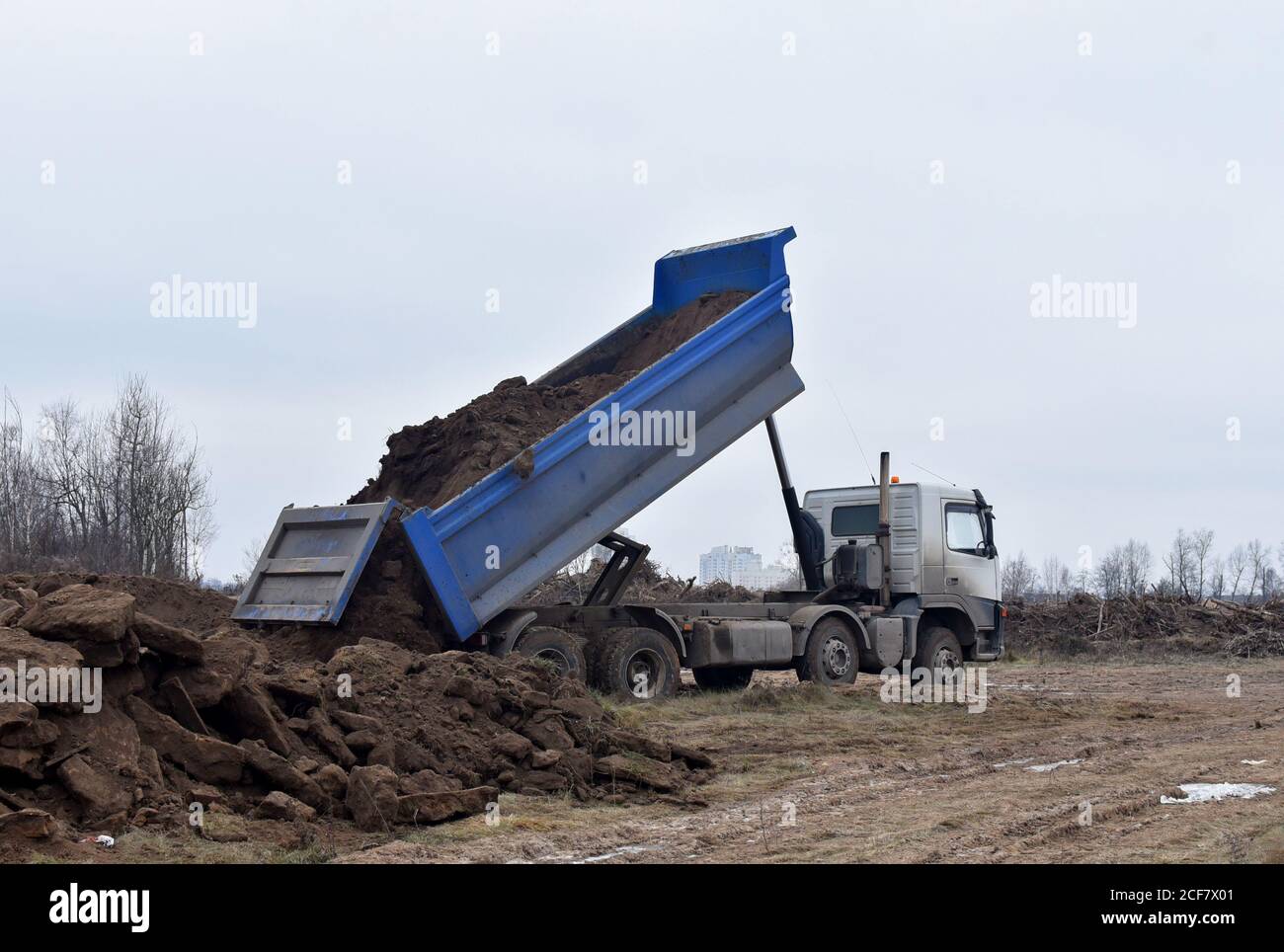 Dump truck dumps its load of sand and ground on construction site for ...