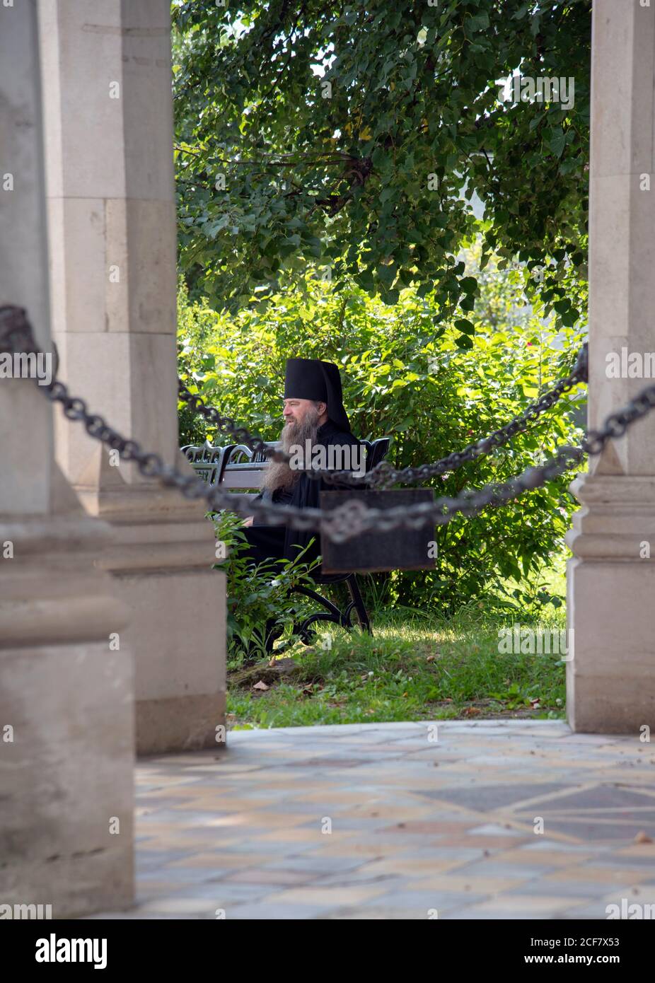 The priest is sitting on a bench behind a stone gazebo Stock Photo - Alamy