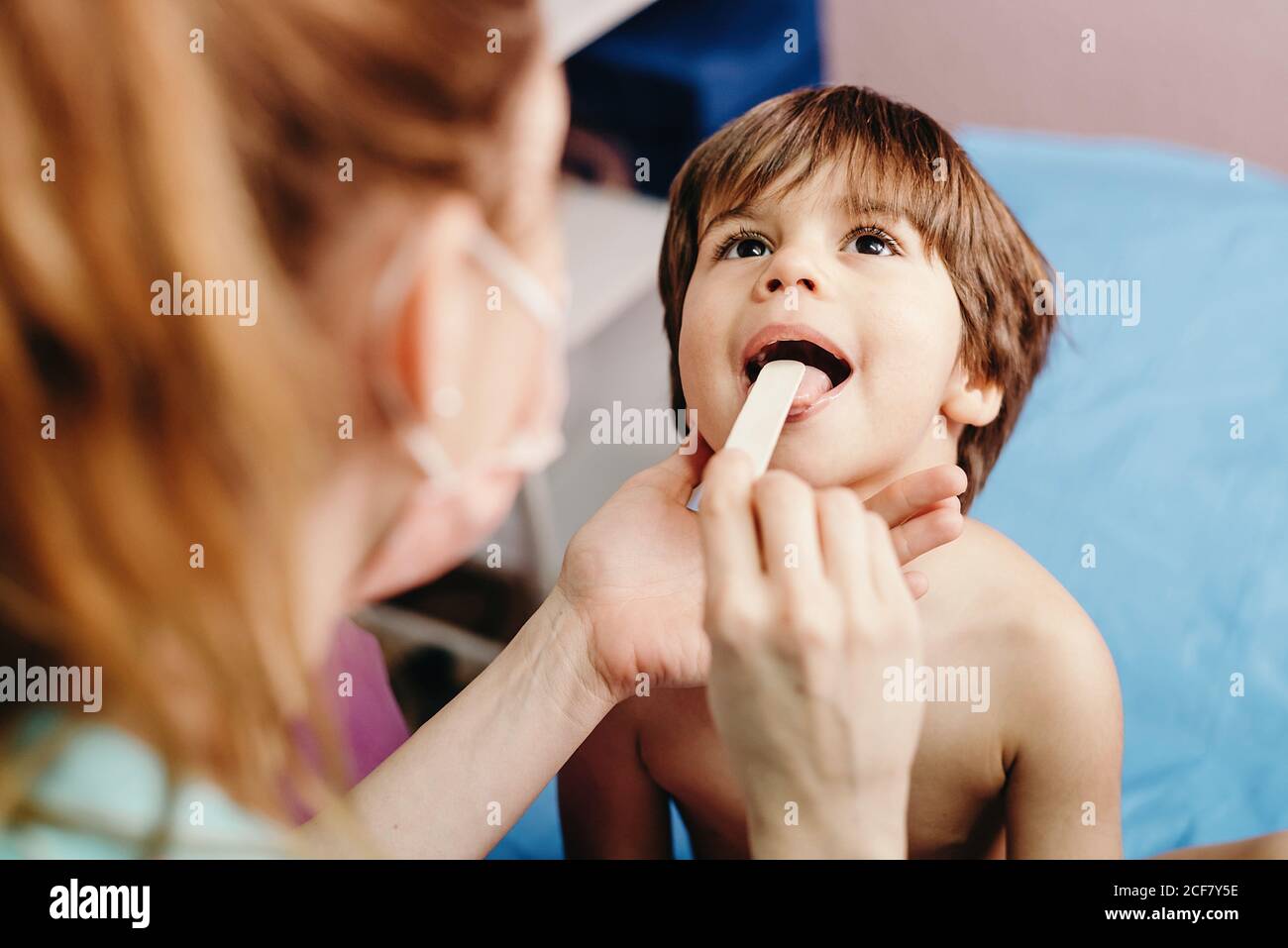 From above of little boy with mouth opened being examined by female ...