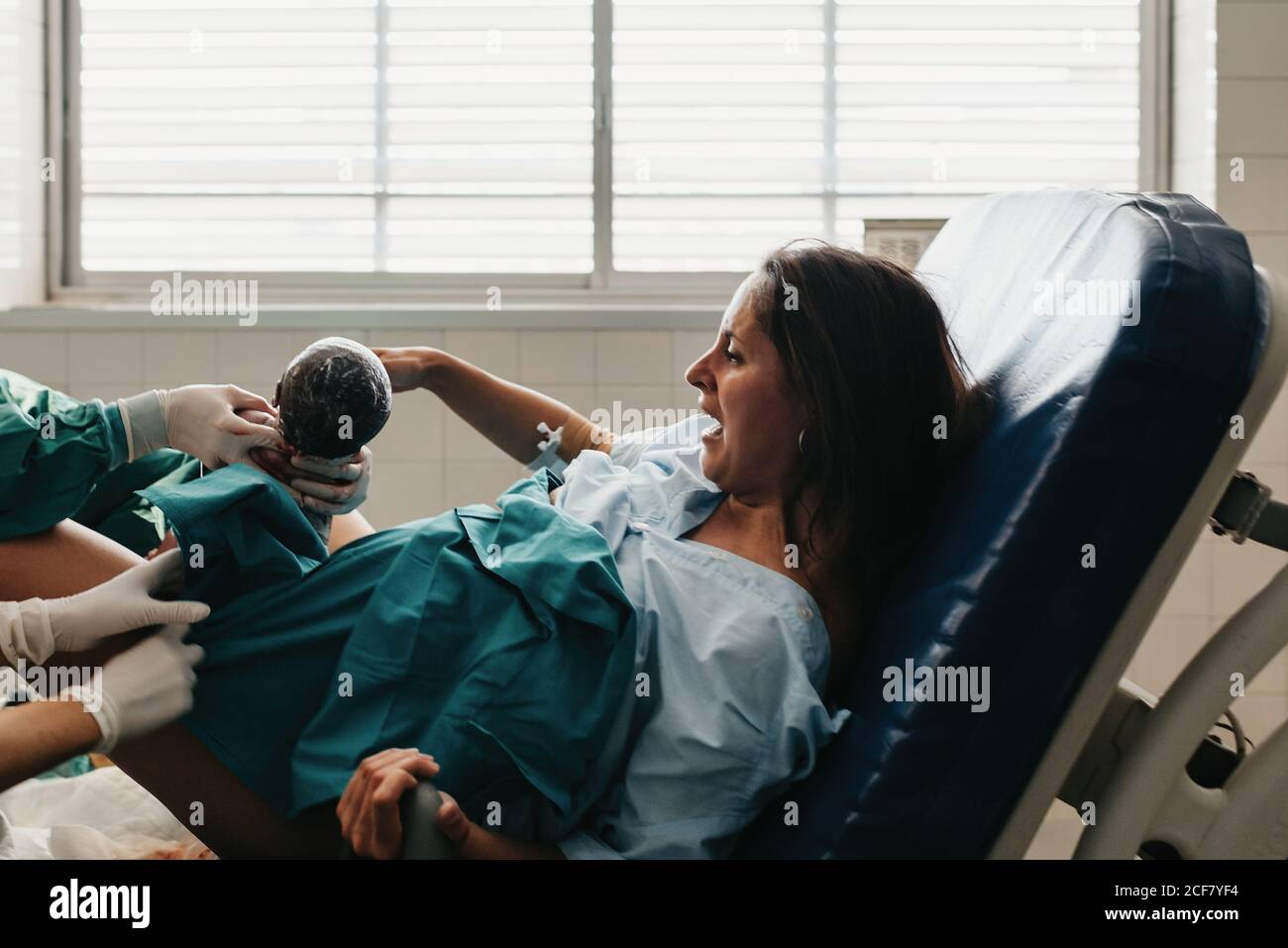 Strained female grasping handle and grunting in pain while giving birth ...