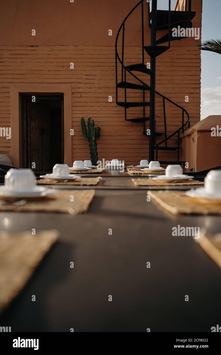 Sunlit terrace of modern restaurant with long table served with tea ...