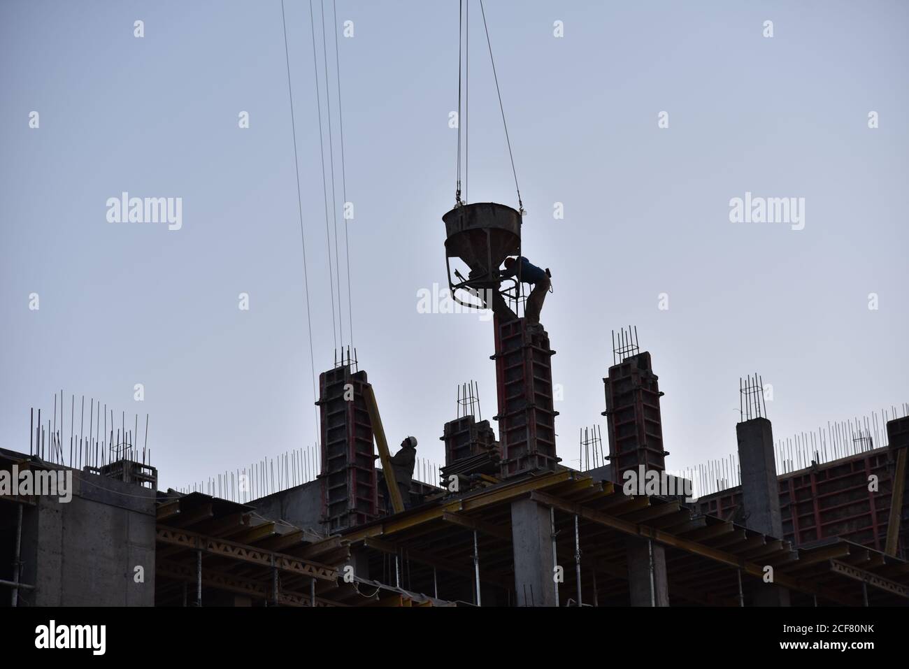 Crane lifting a concrete bucket on sunset background. Silhouettes of ...