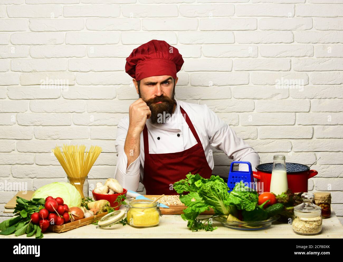 Chef prepares meal. Man with beard holds chin on white brick wall ...