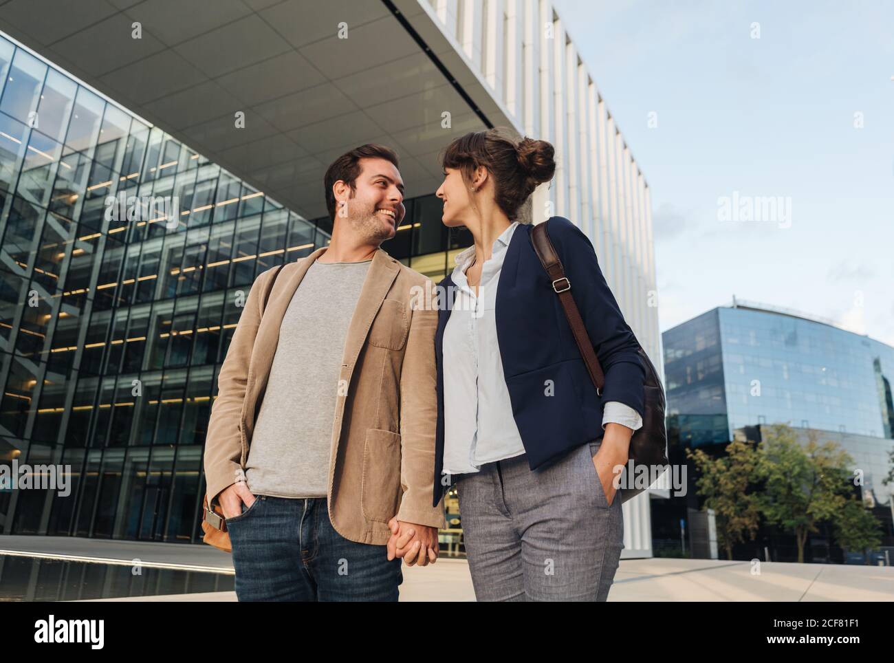 From below happy couple coworkers in casual outfits smiling and walking ...