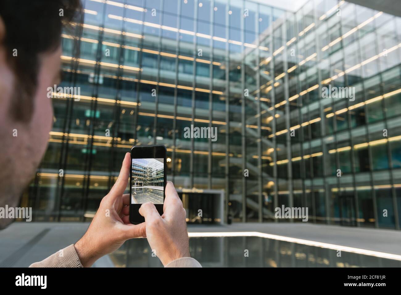 Back view of crop adult male photographing transparent glass facade of ...