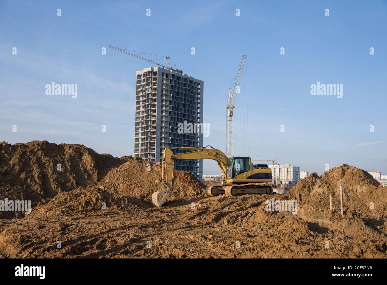 Yellow excavator on the background of tower cranes and high-rise ...