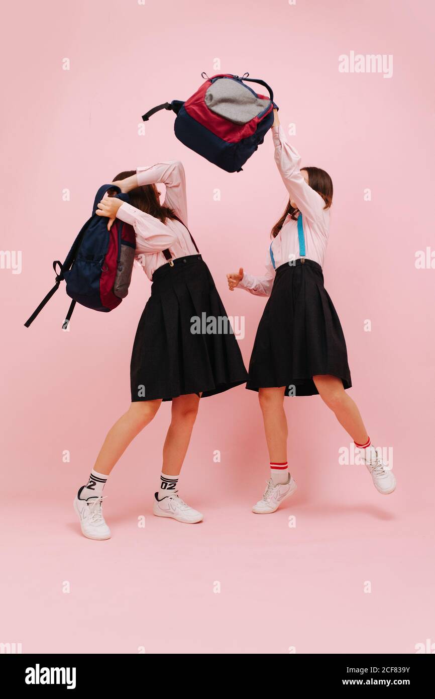 Happy little twin schoolgirls fighting with their backpacks. Low angle ...