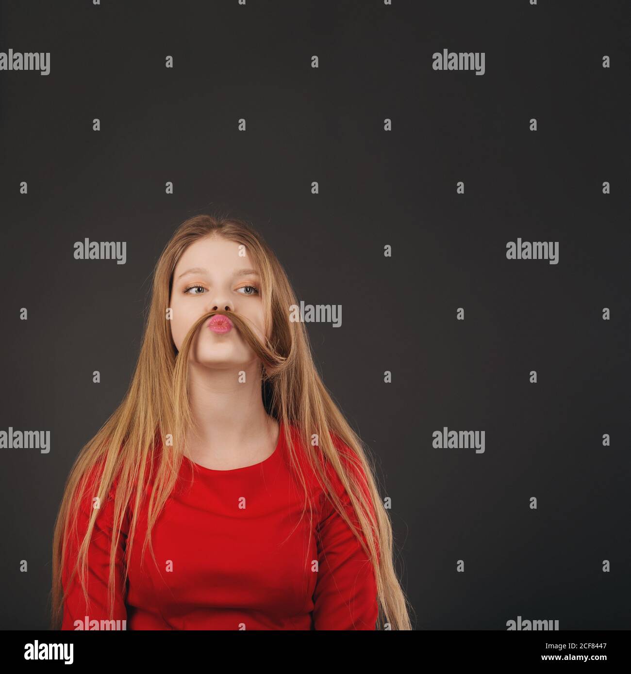 Cool young blonde Caucasian woman making mustache with her hair. Beautiful teenage girl making ...