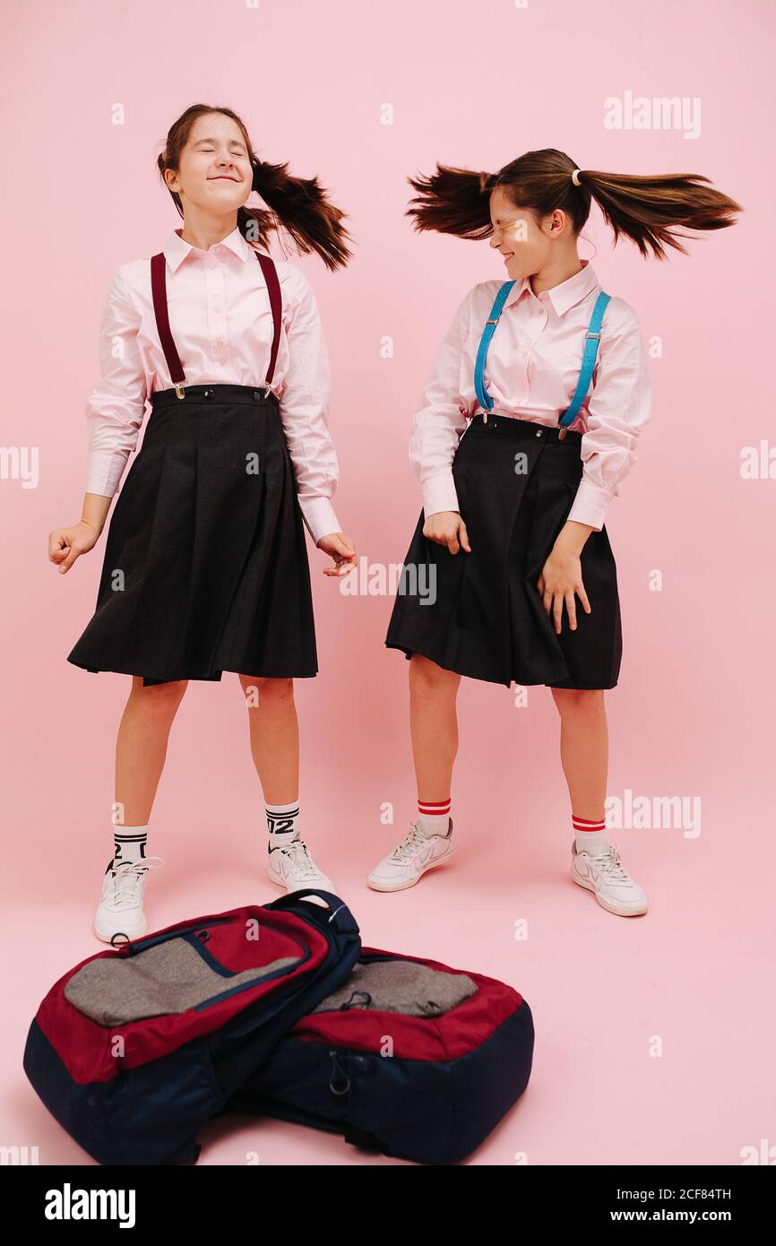 Happy little twin schoolgirls with twintails shaking heads. Low angle ...
